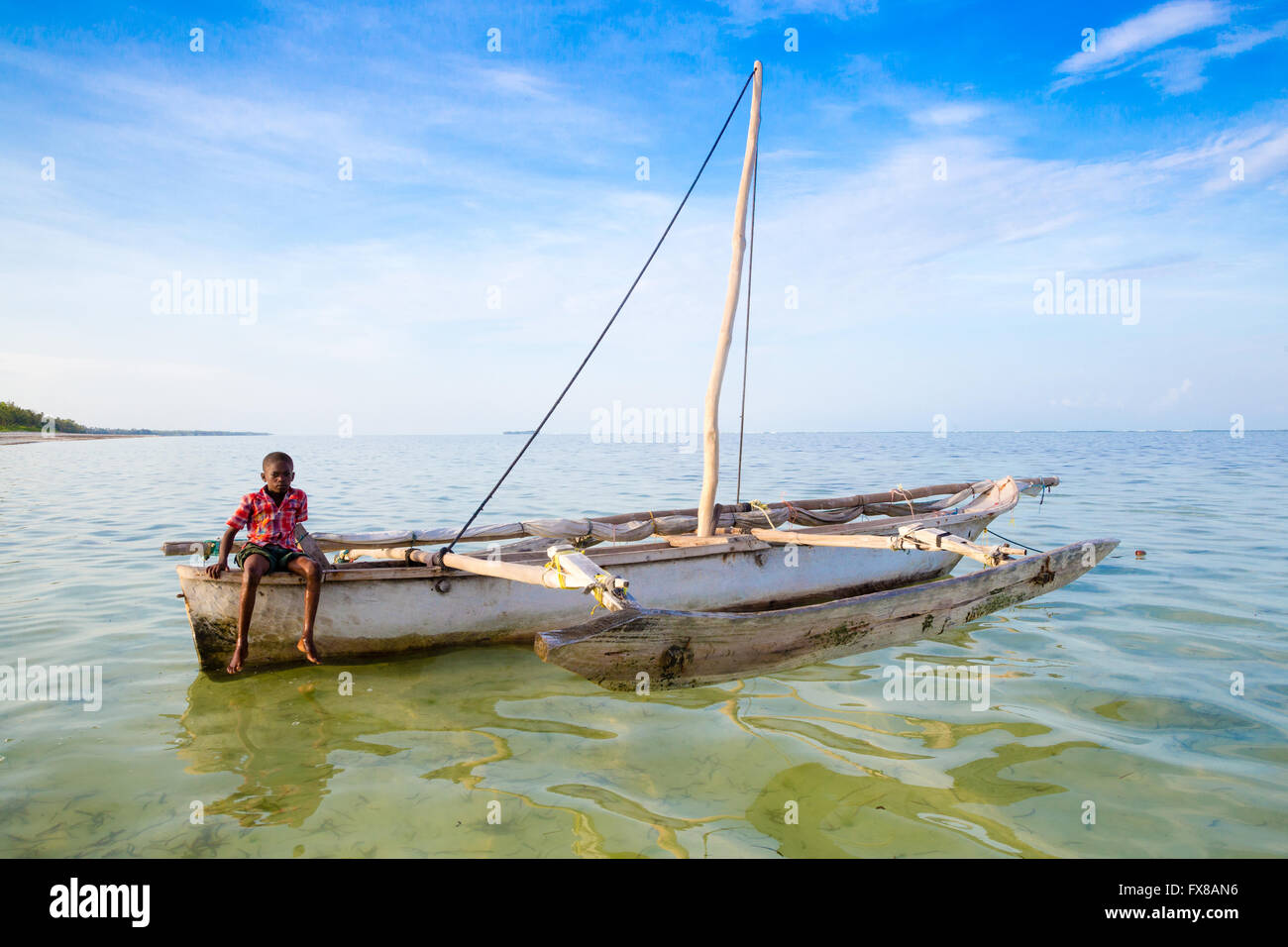 A young boy sits on the stern of a small dhow on the coast of Zanzibar ...