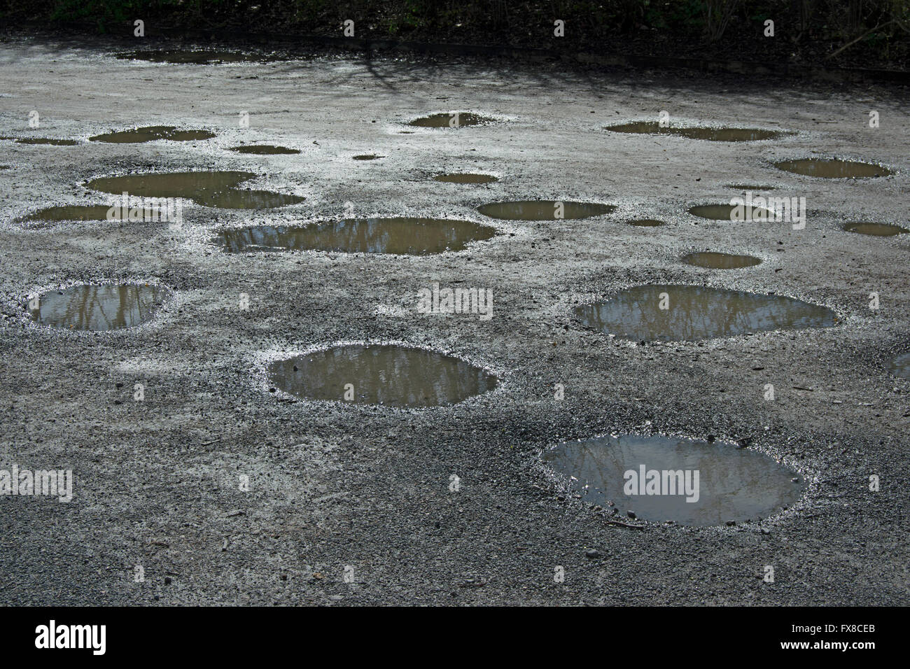 puddles formed in the surface indentations of a tarmacked car park ...