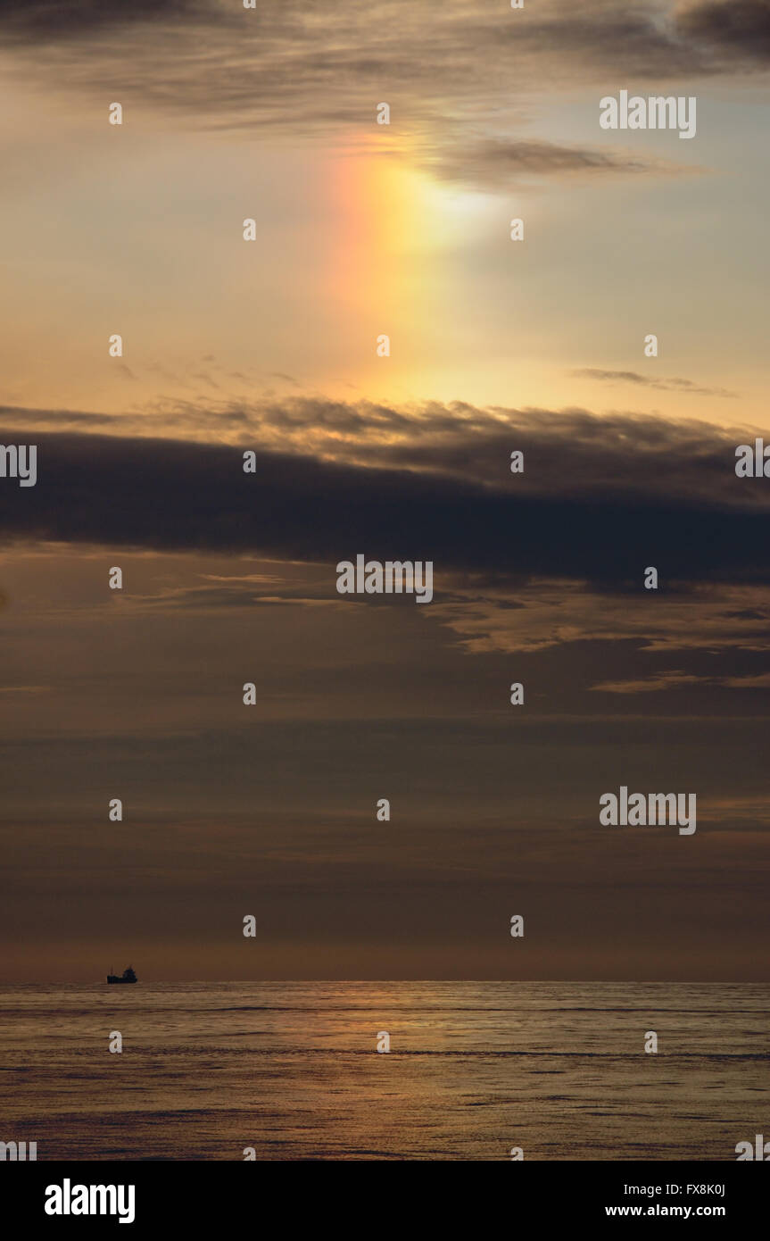 Seascape and rainbow coloured cloud in evening sunshine Stock Photo - Alamy