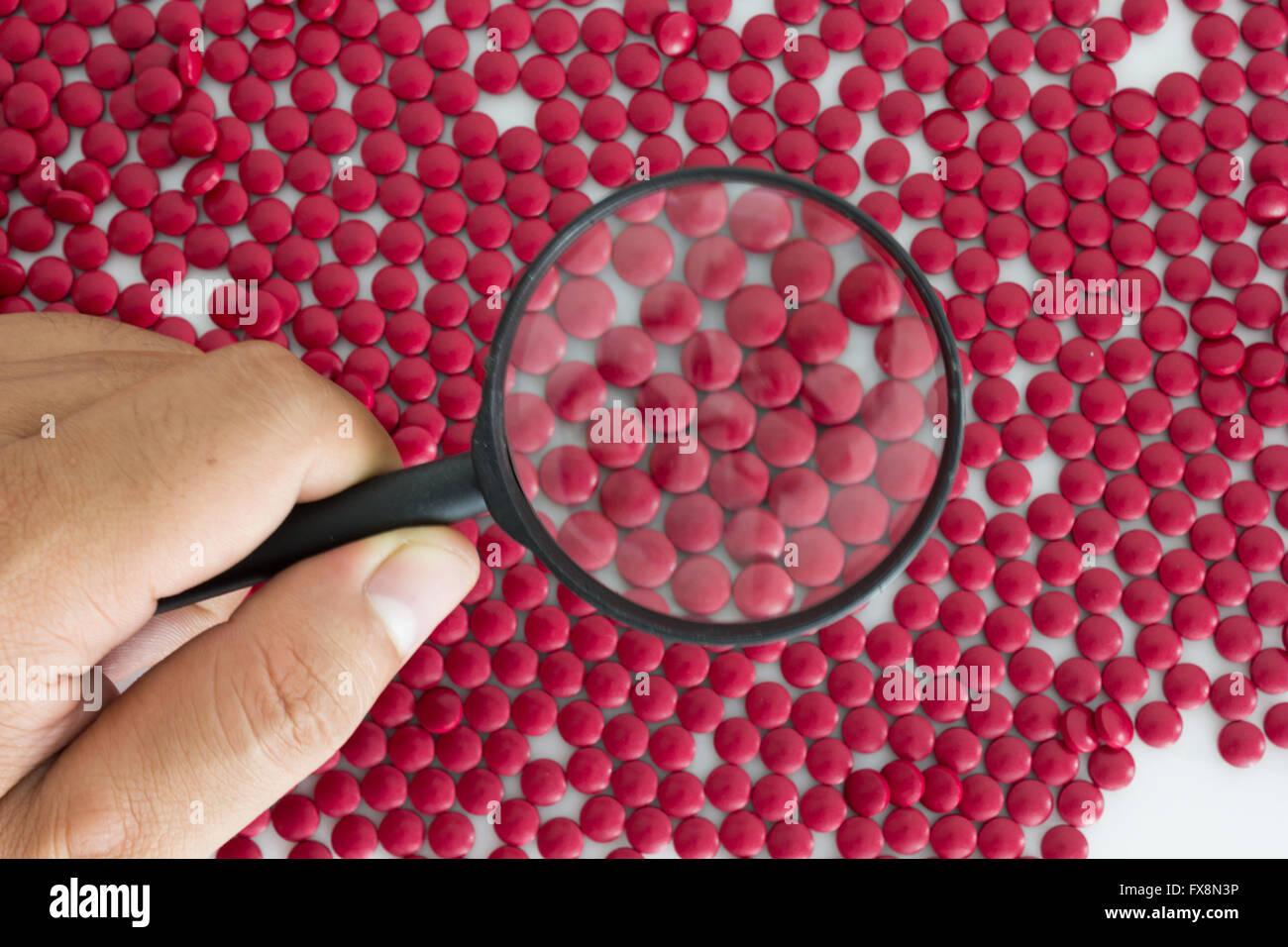 Hand Holding Magnifying Glass on red drugs Stock Photo - Alamy