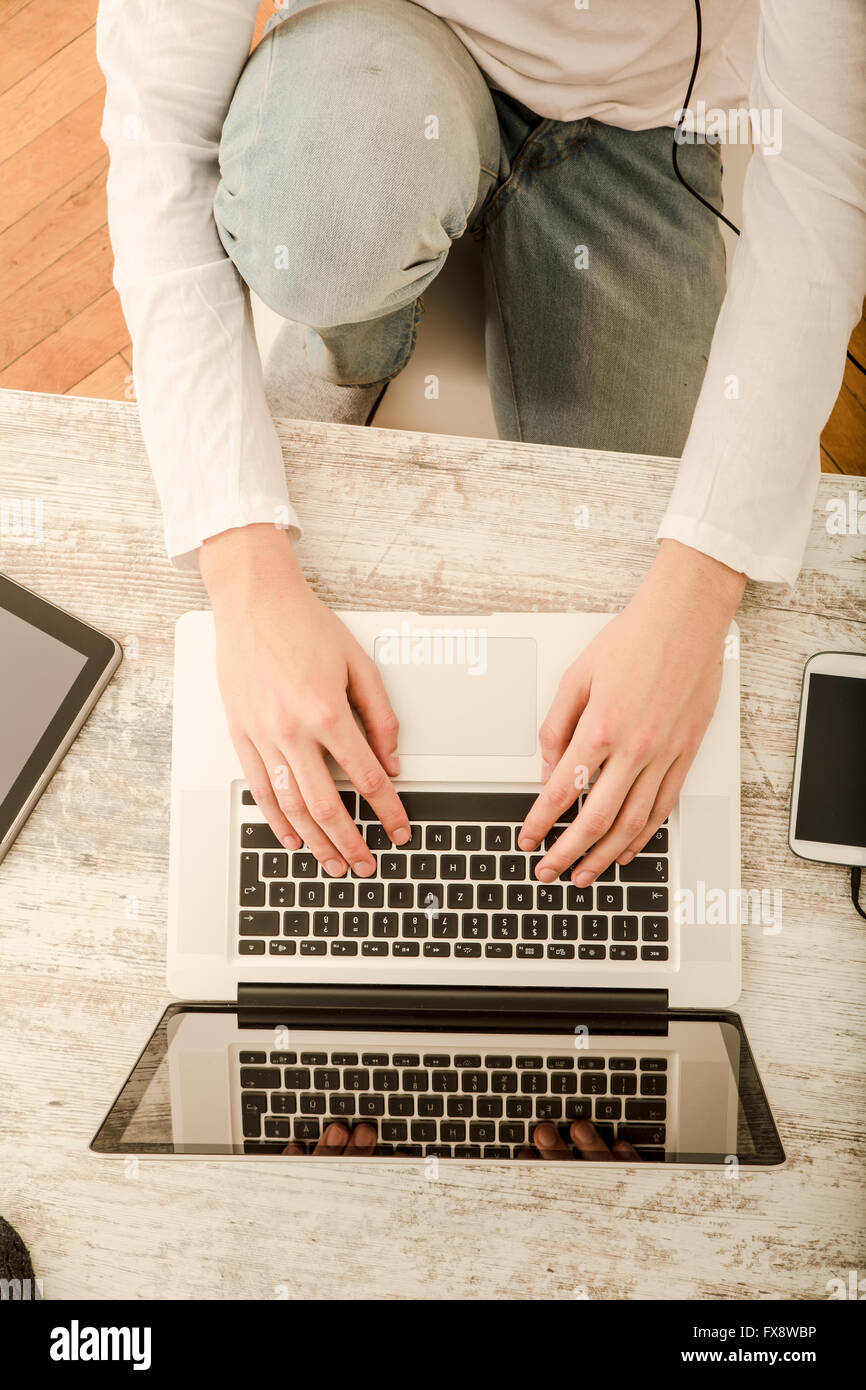 A young man using his laptop computer and various other devices on a ...