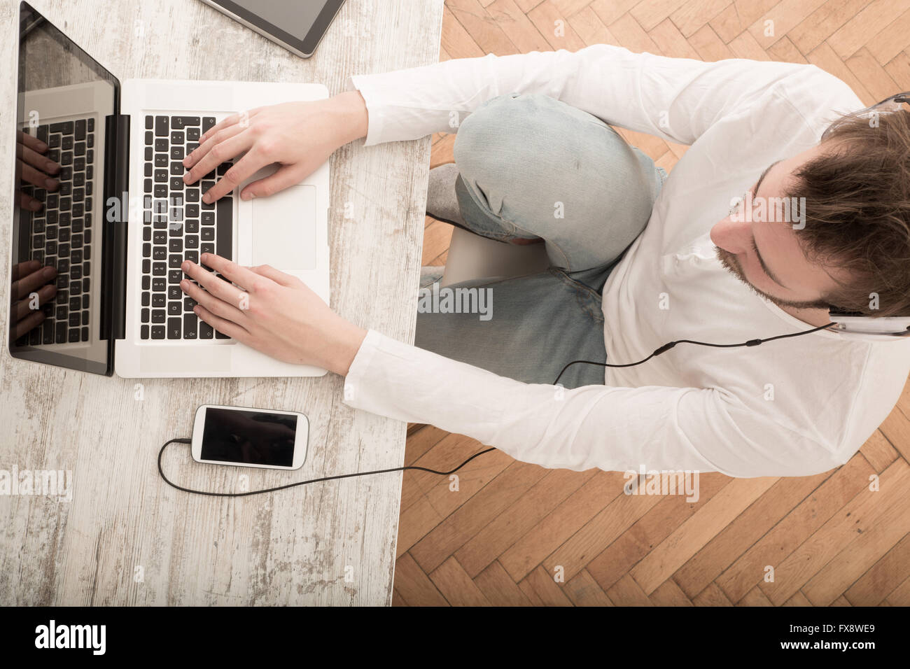 A young man using his laptop computer and various other devices at home ...