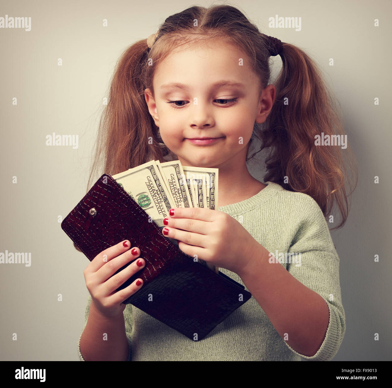 Cute happy kid girl holding wallet and looking on dollars and think how ...
