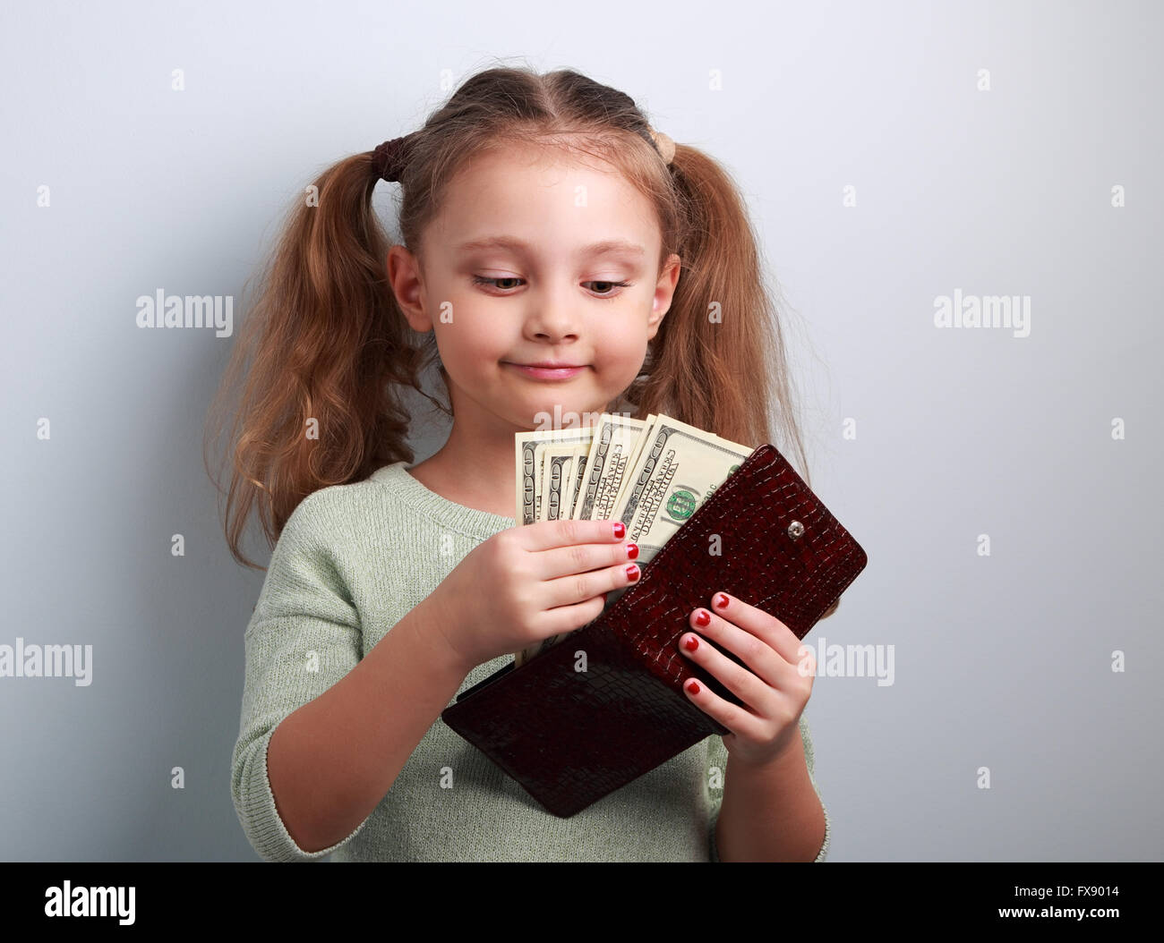 Cute happy kid girl holding wallet and looking on dollars and think how ...