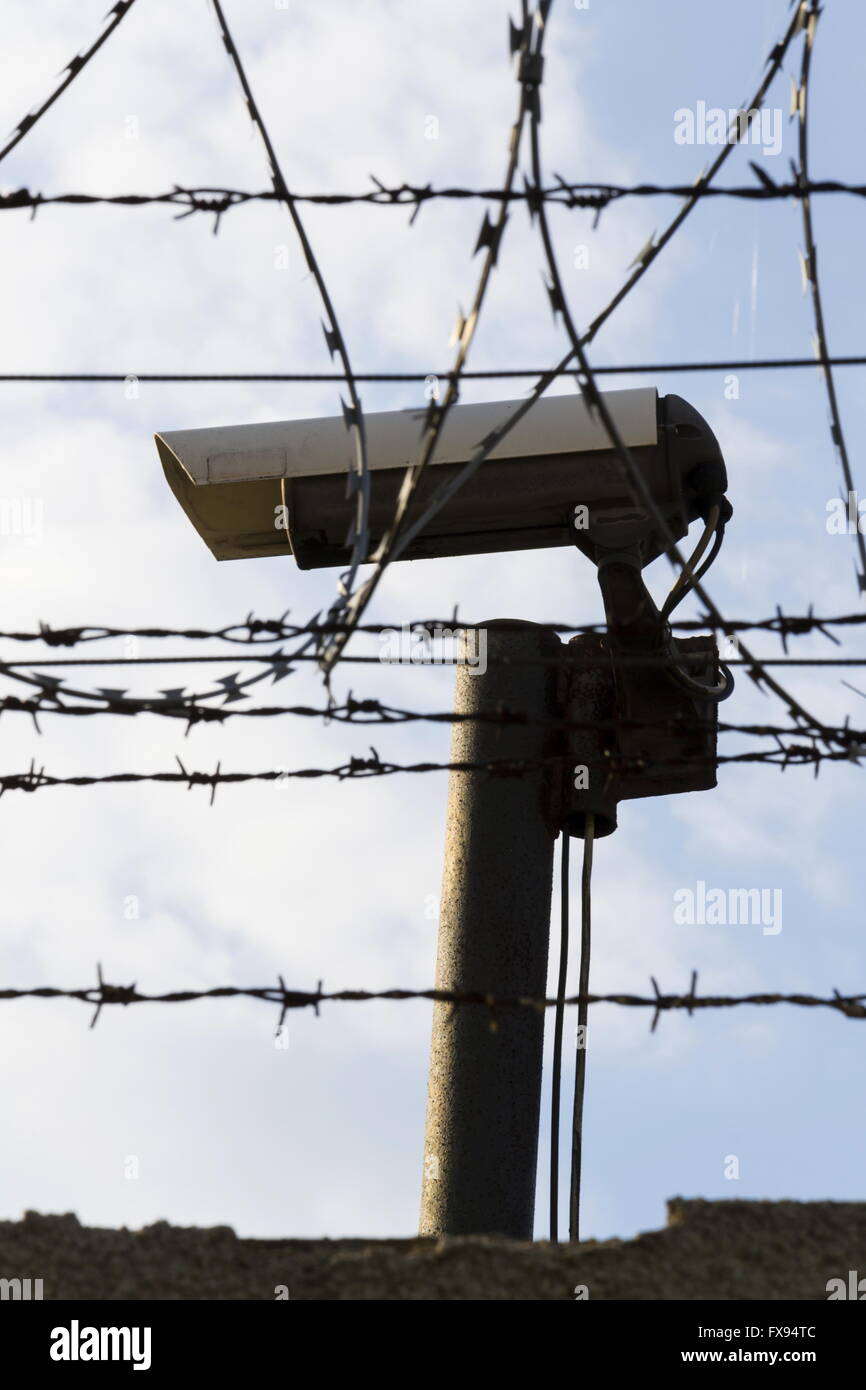 Security camera behind barbed wire fence stretched around prison walls ...