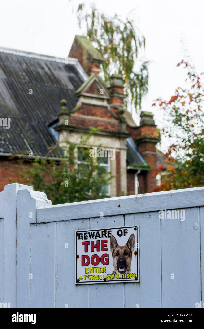A Beware of the Dog sign on a tall wooden gate outside a large house ...