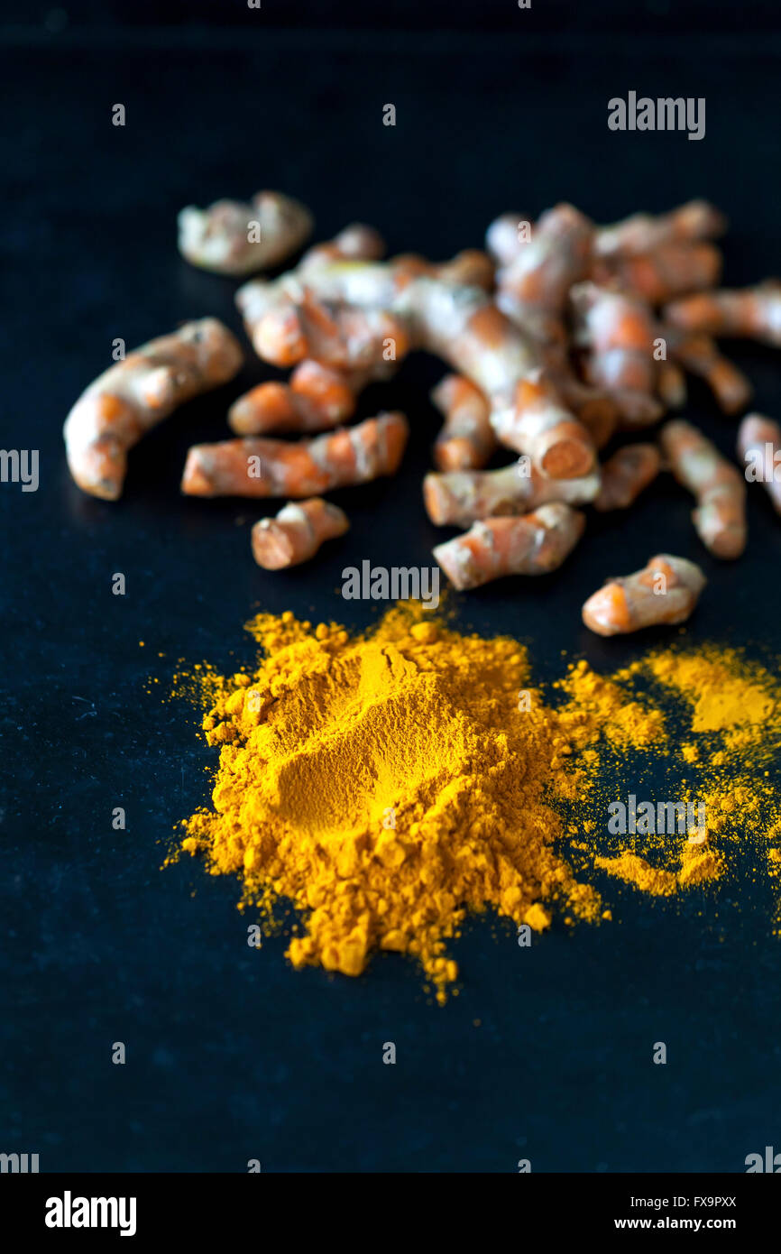 Fresh turmeric (curcuma) and ground yellow turmeric powder on the black ...