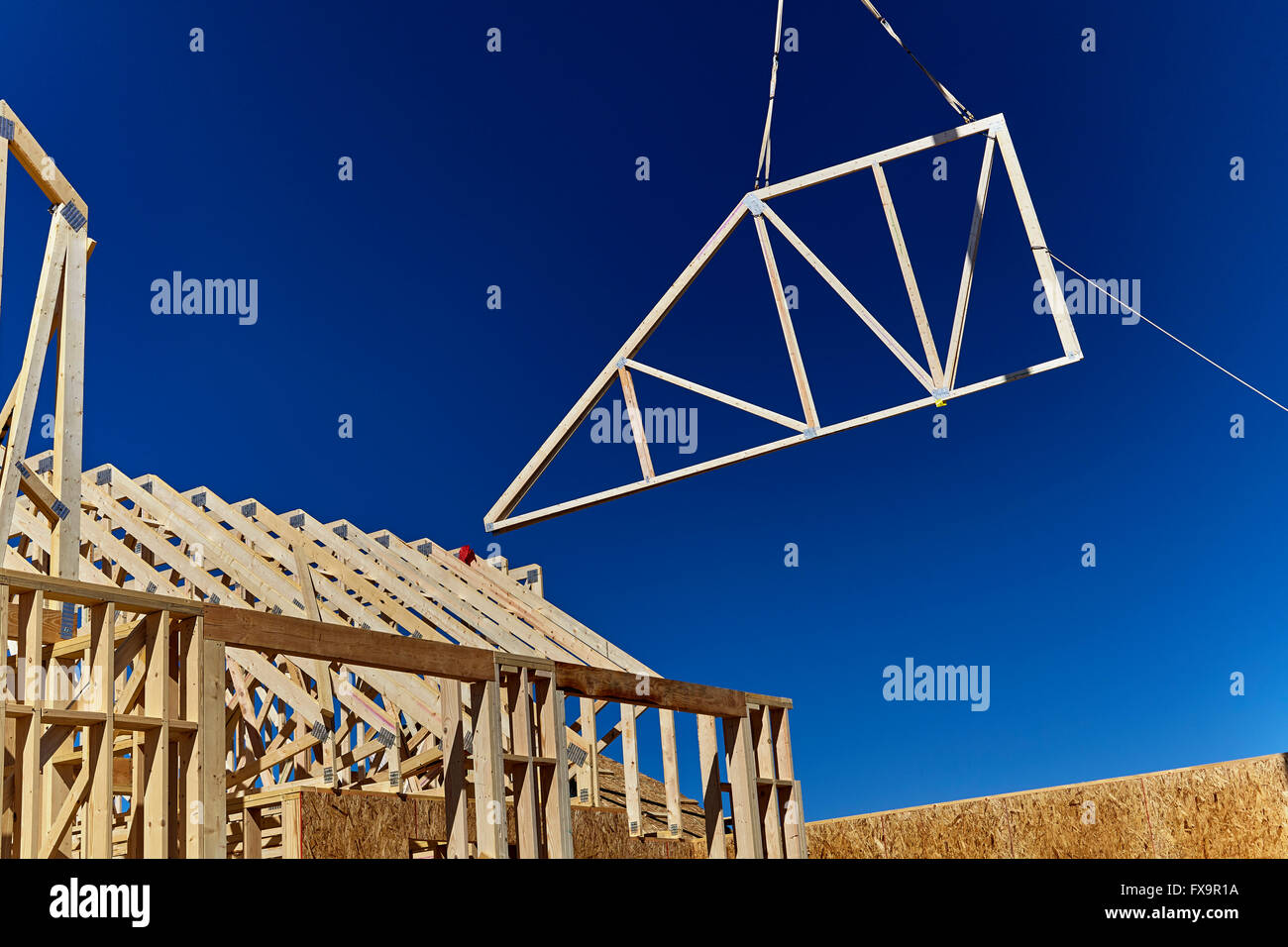 A wooden roof truss being lifted by a crane in the air for placement on ...