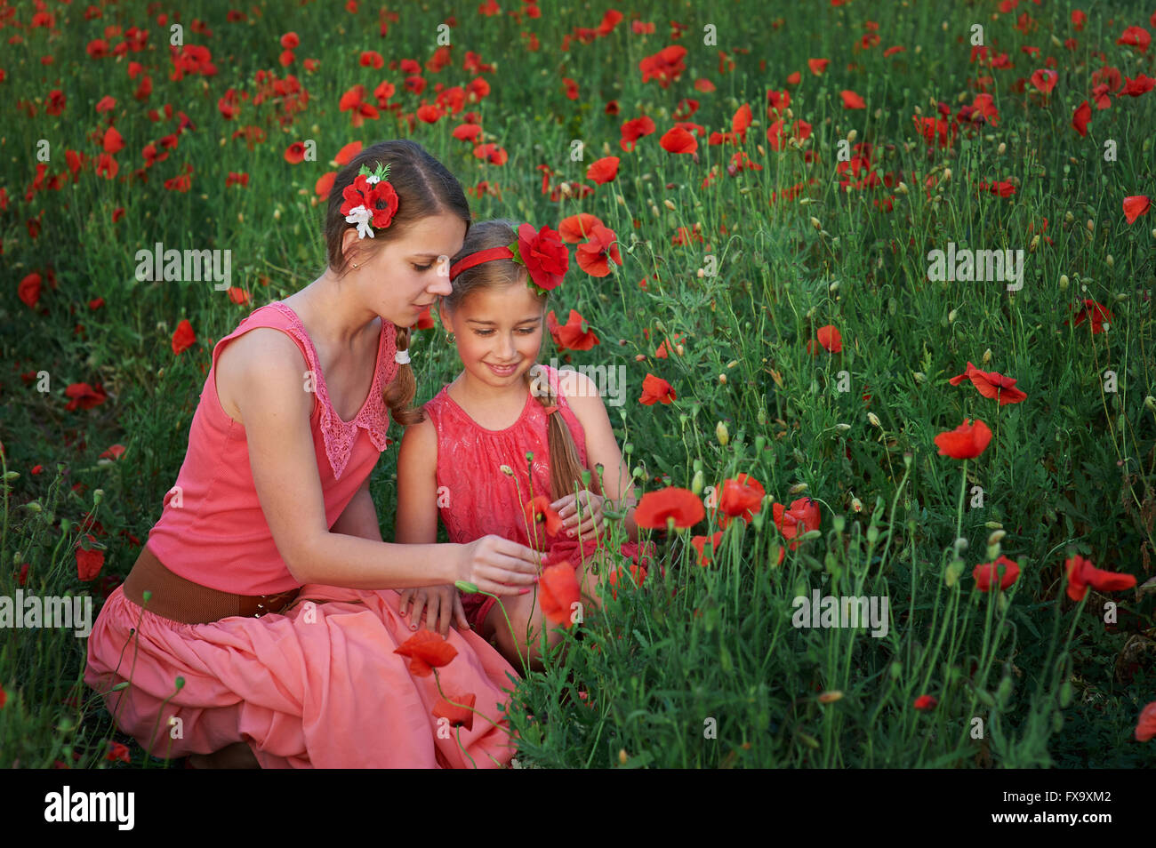two girls in red dress walking on poppy field Stock Photo - Alamy