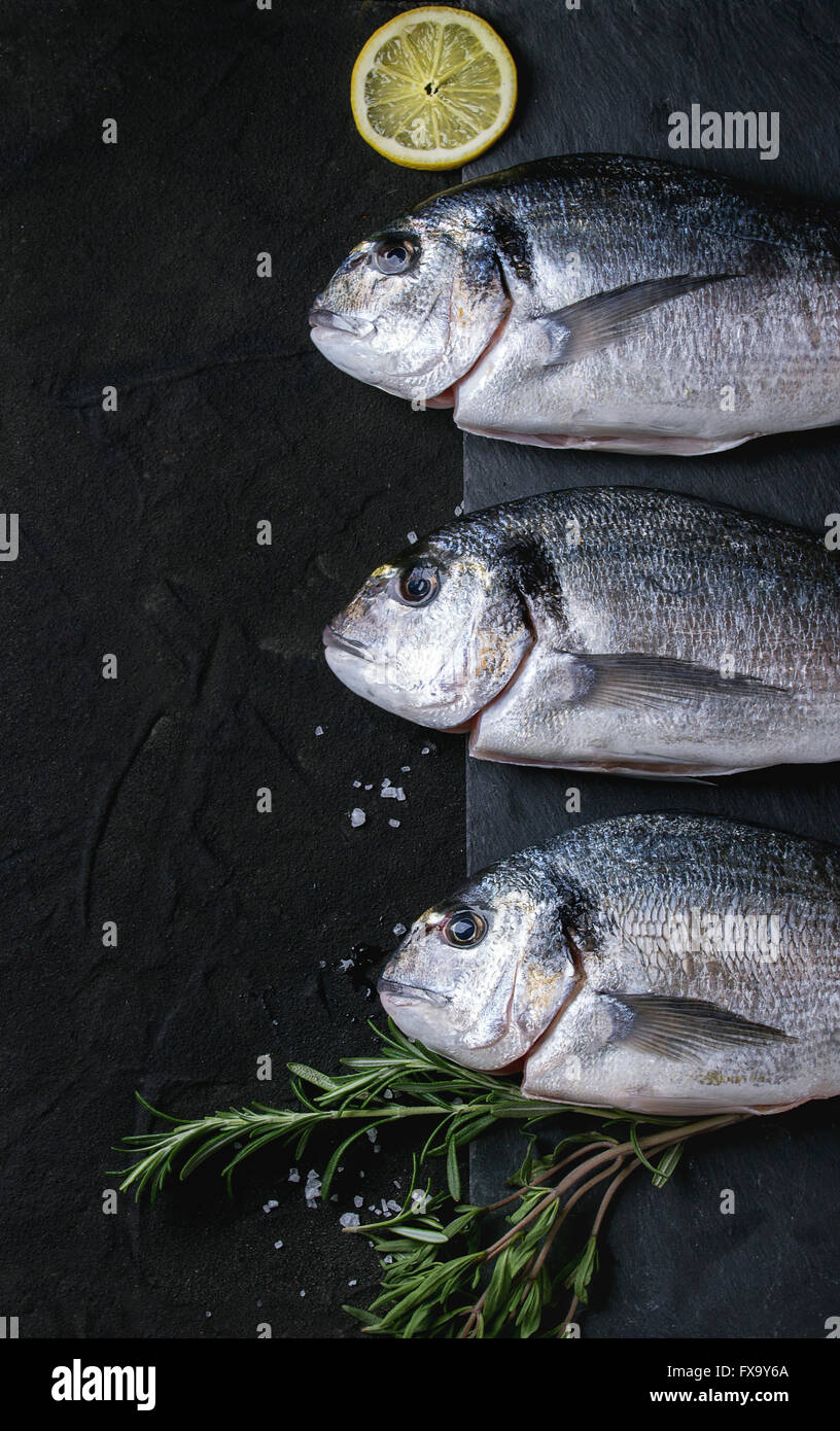 Three ready to cook raw bream fish with herbs, lemon and olive oil on ...