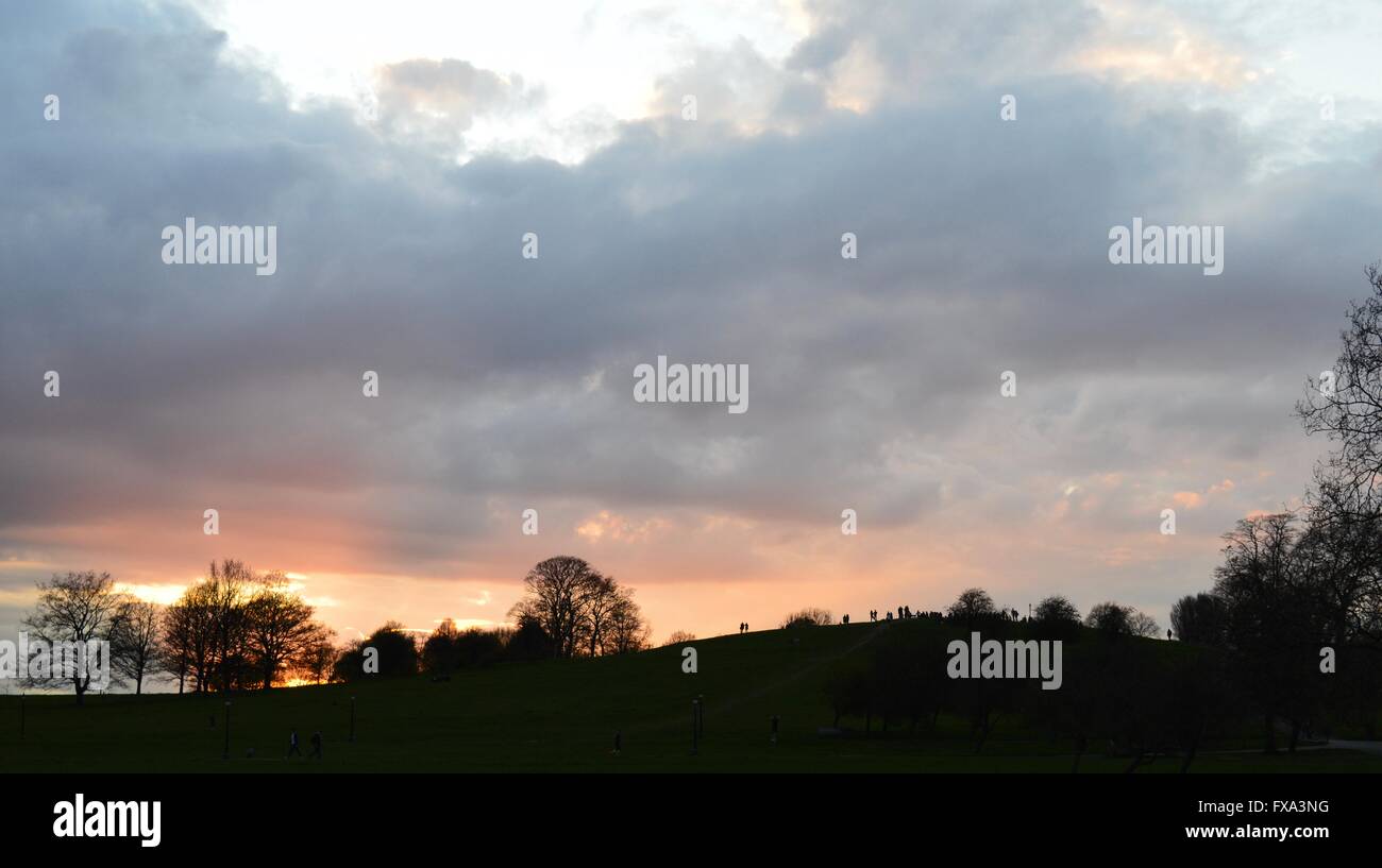 A dramatic sunset, orange sky with grey clouds, with trees and people ...