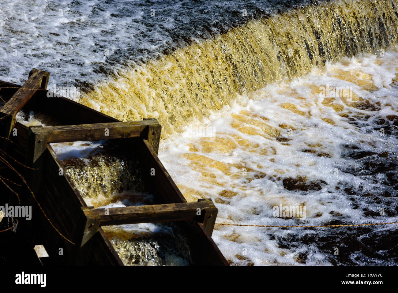 Wooden fish ladder with flowing water beside a reservoir overflow. This ...