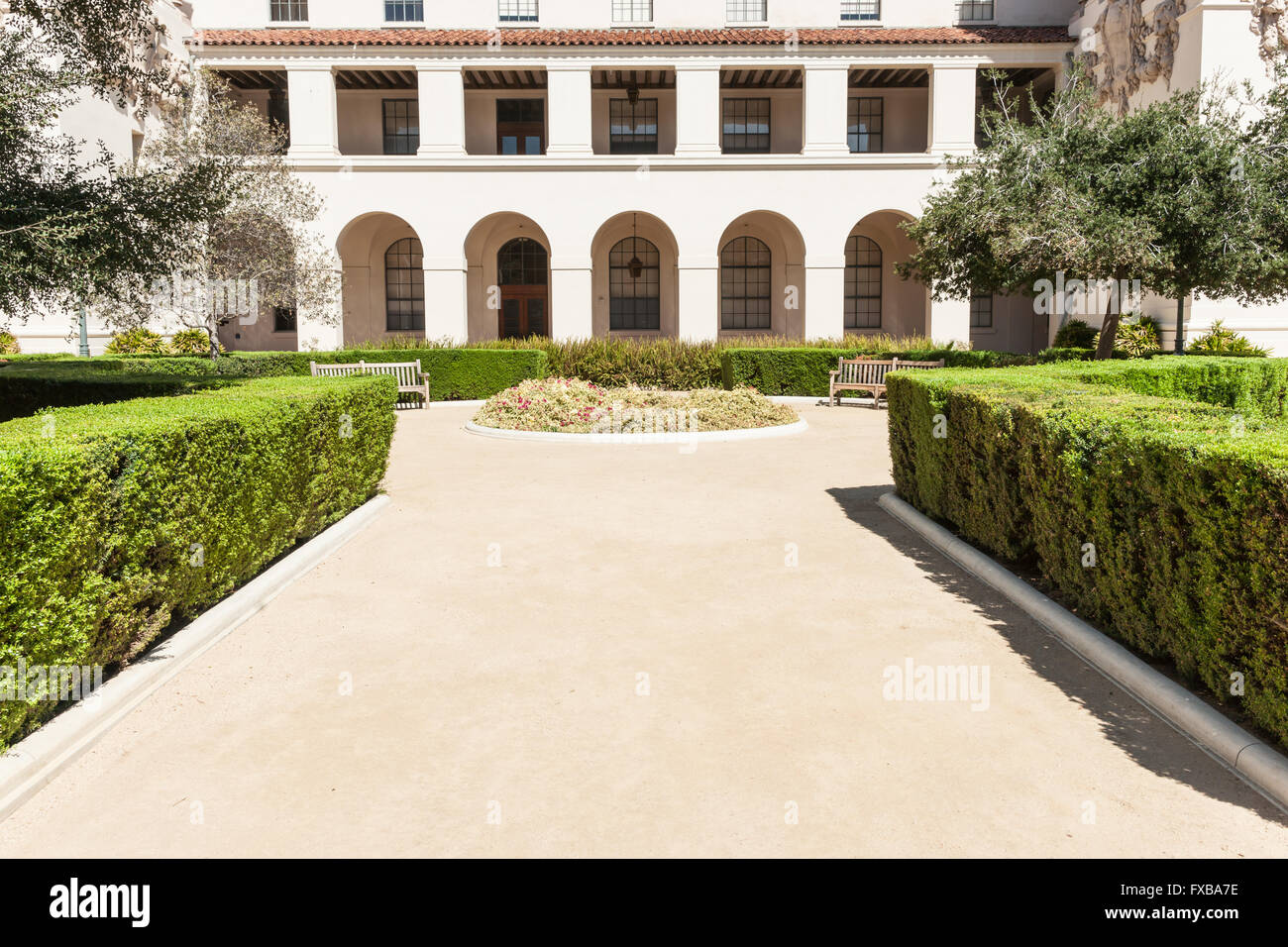 Courtyard path lined with manicured hedge leads to round and garden ...