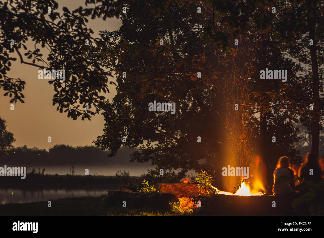 A long exposure of a campfire next to a river, with people gathered ...
