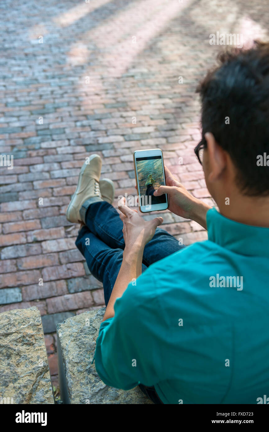 Young asian man taking photo of street and his feet with mobile phone ...