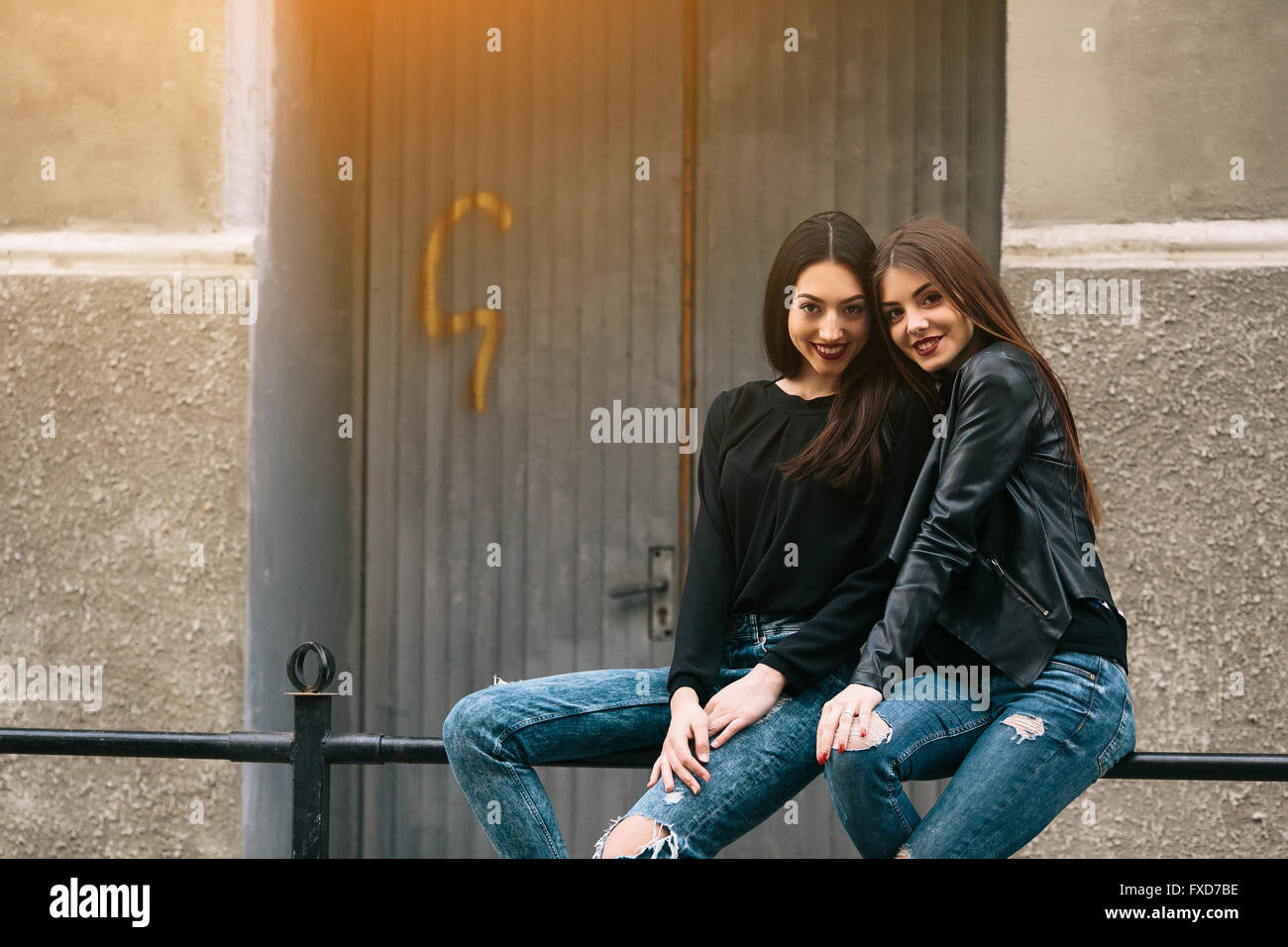 Two young adult women sitting on the railing and posing for the camera ...