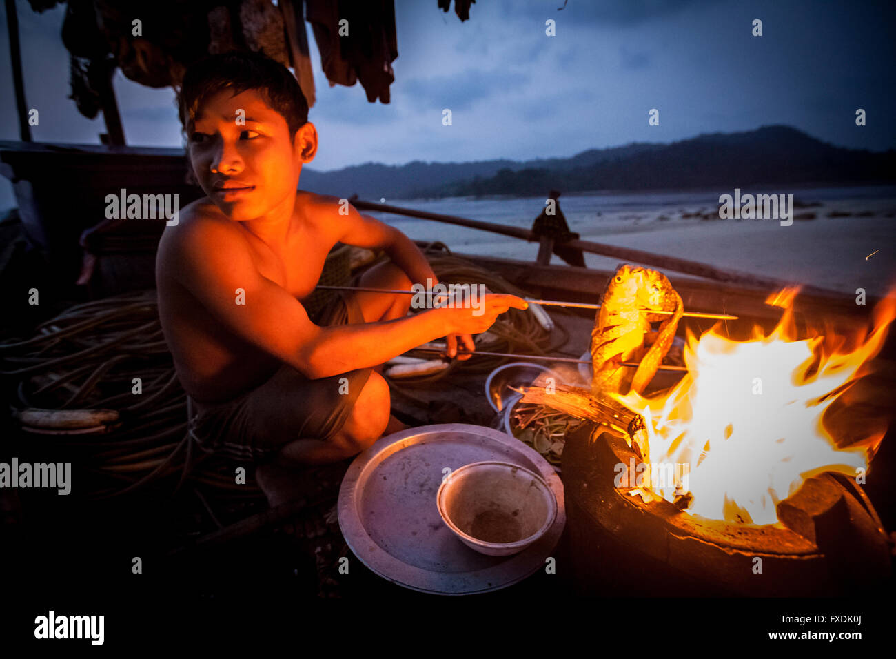 Myanmar, Asia, a boy is cooking fish on the beach using fire Stock ...