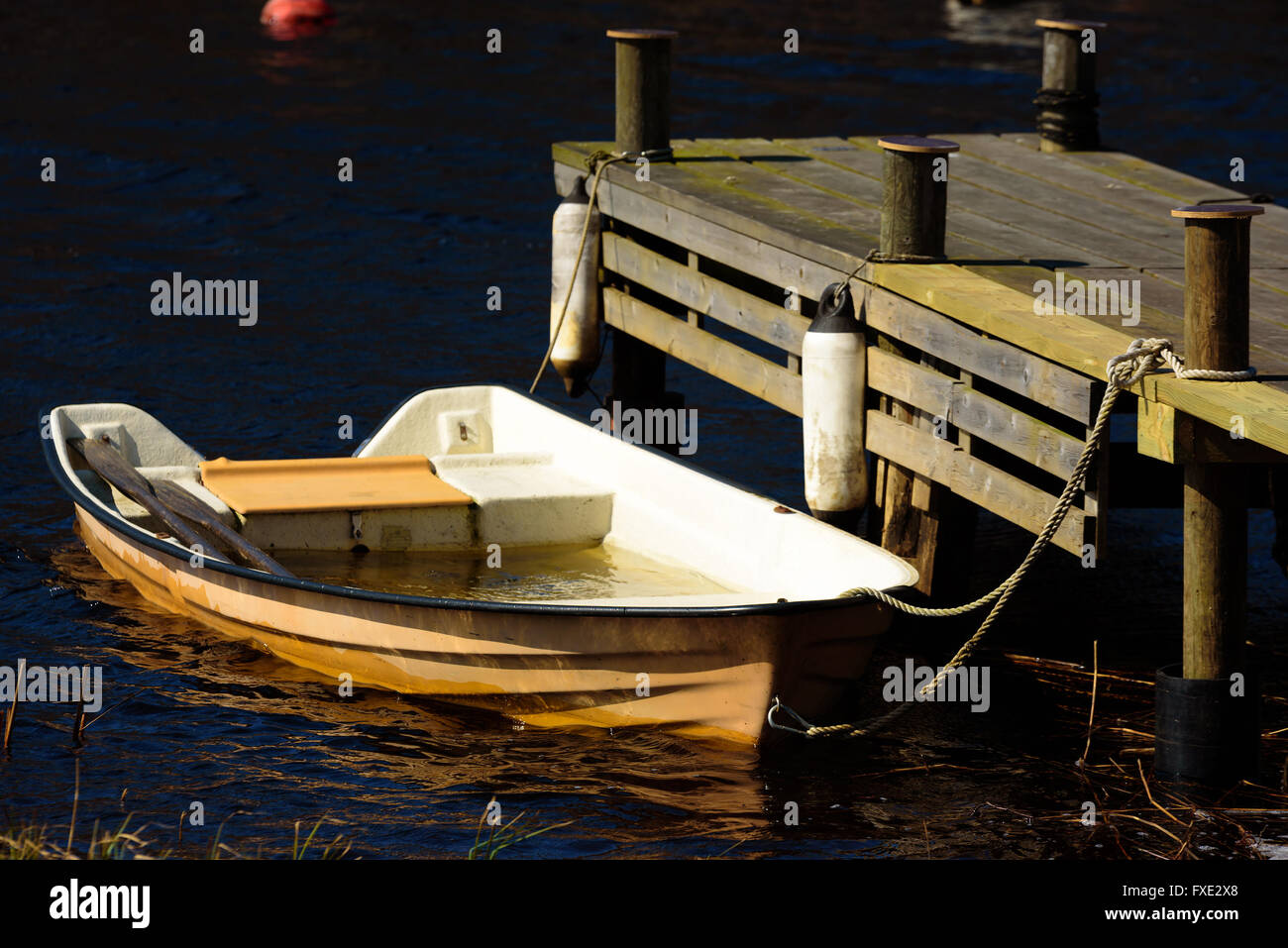 Orange plastic rowboat filled with water moored at a wooden pier in ...