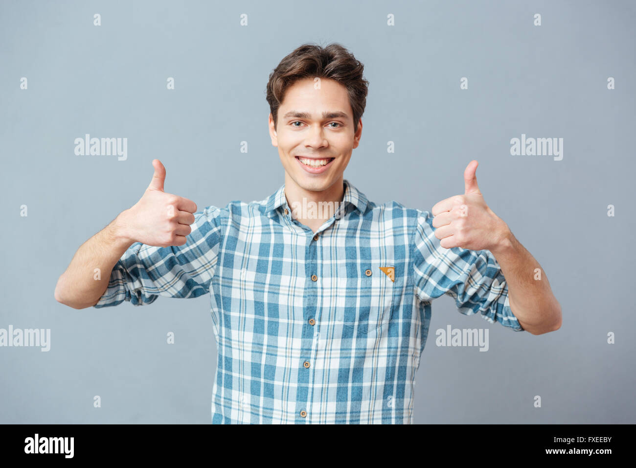Happy casual man showing thumbs up over gray background Stock Photo - Alamy