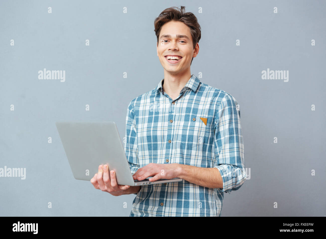 Laughing man standing with laptop computer over gray background and ...