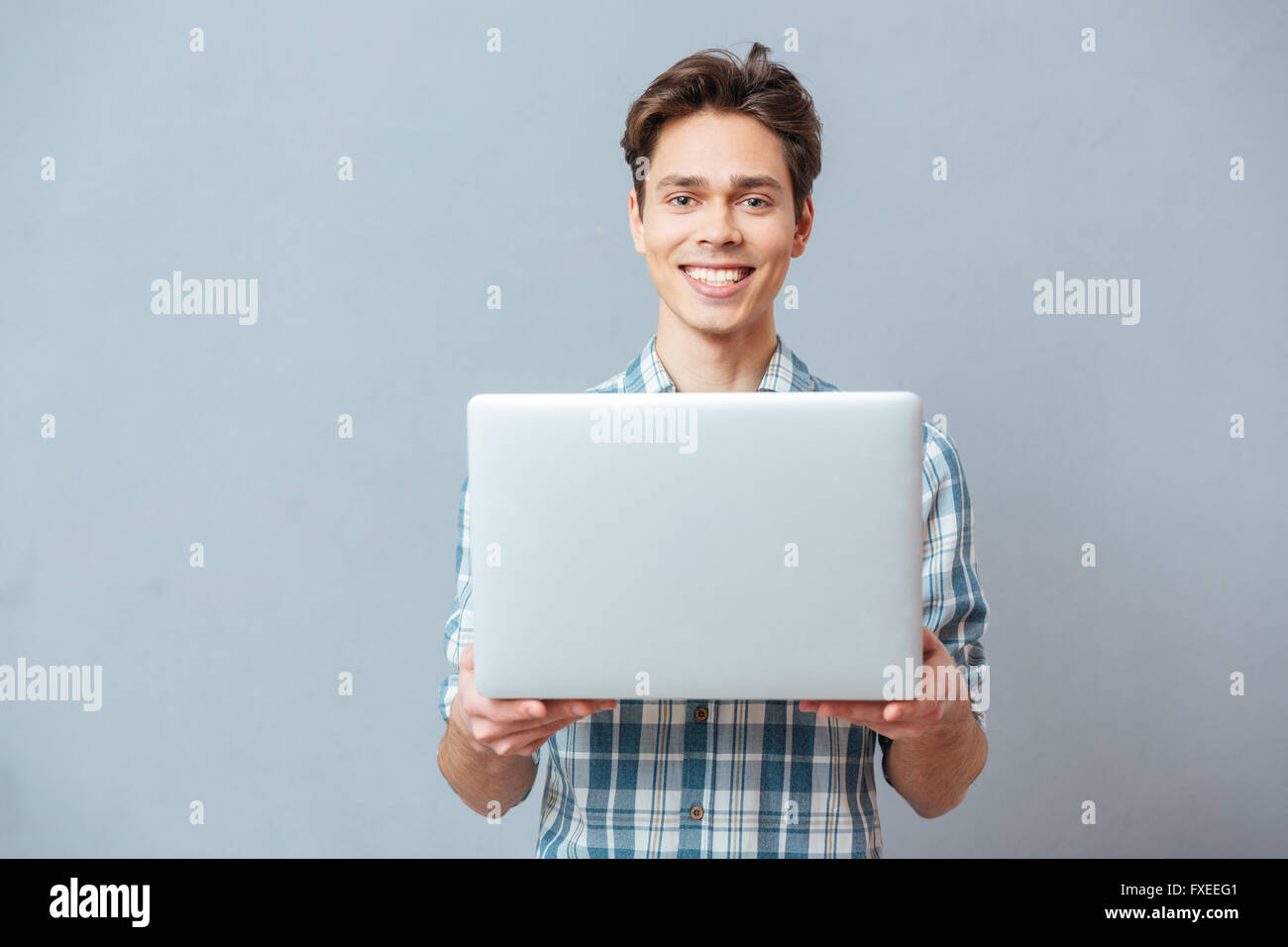 Happy casual man standing with laptop computer over gray background ...