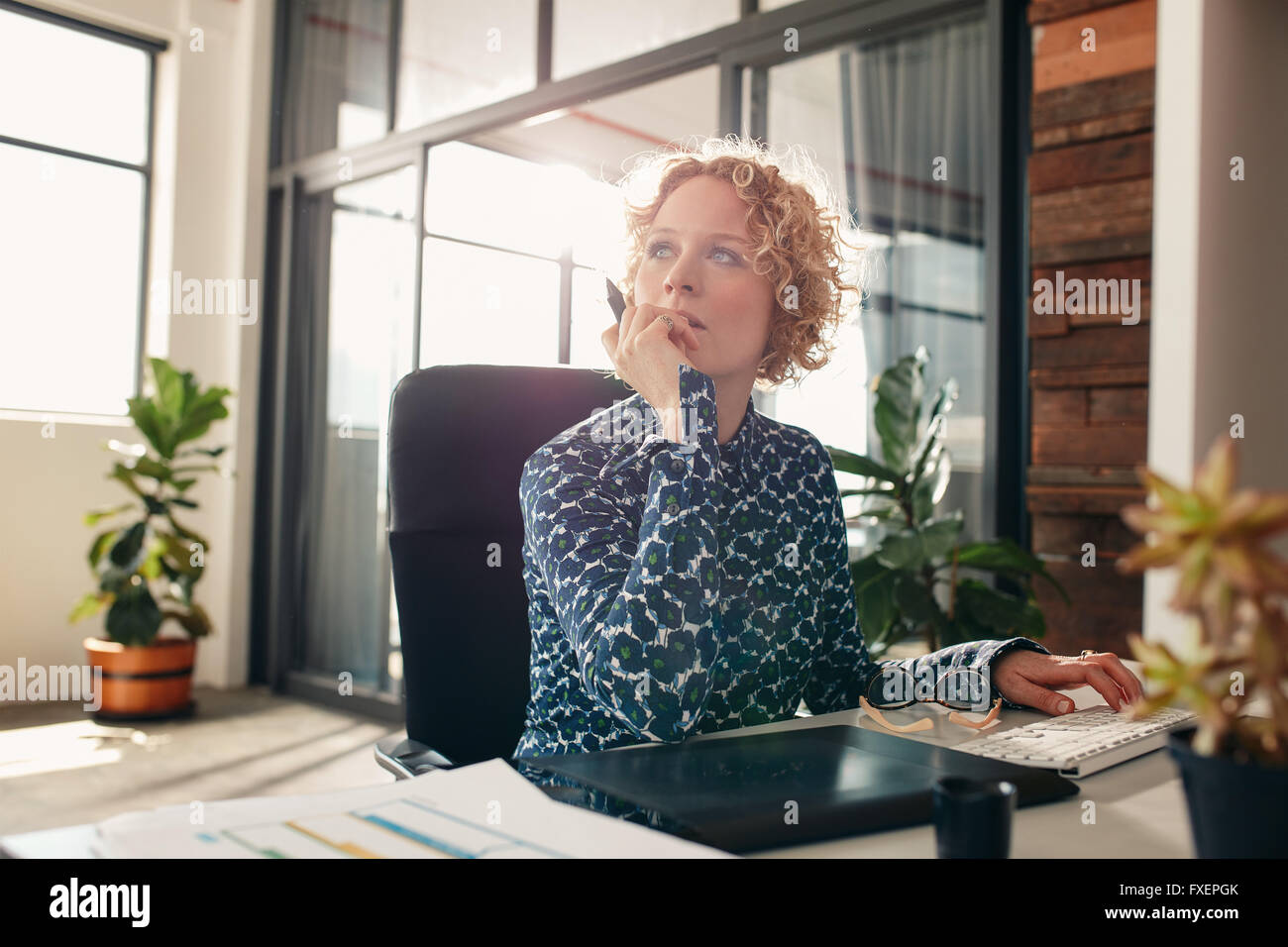 Portrait of young female designer sitting at her desk looking away and ...