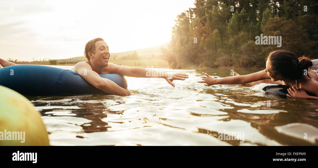 Loving young couple about to hold hands while floating on inner tubes ...