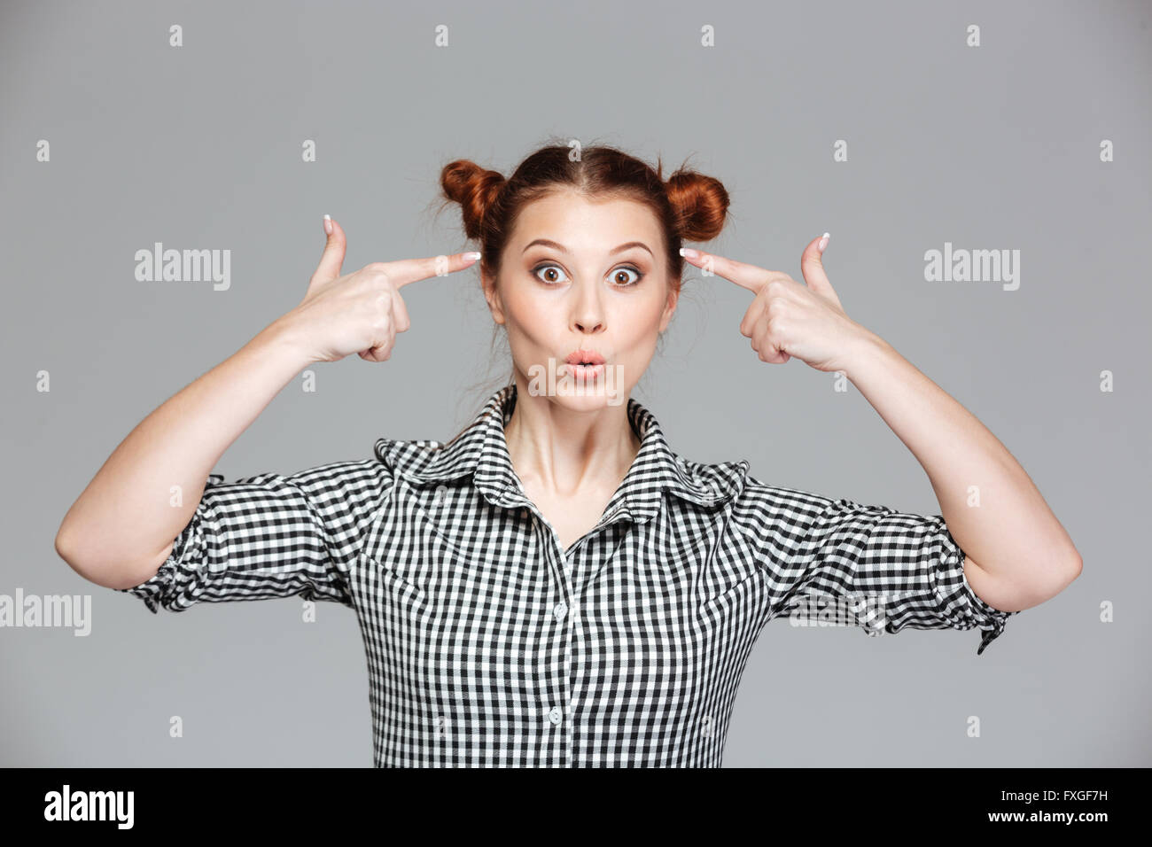 Joyful comical young woman pointing on her temples and making funny ...
