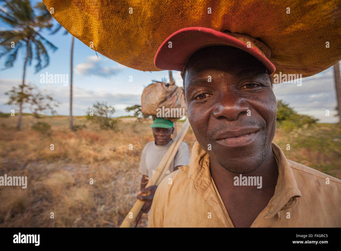 Mozambique, a smiling man in palm plantation with carriage on the head ...