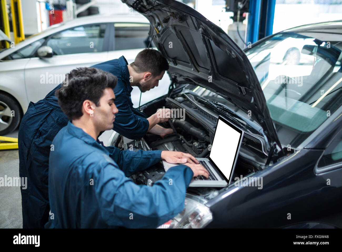 Mechanics examining car engine using laptop at the repair garage Stock ...