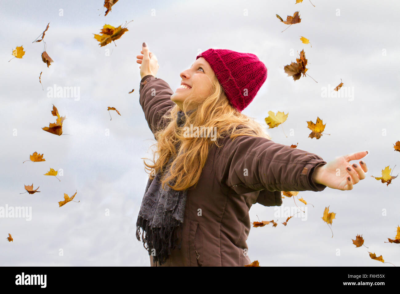 Autumn leaves falling on happy young woman with raised arms Stock Photo ...