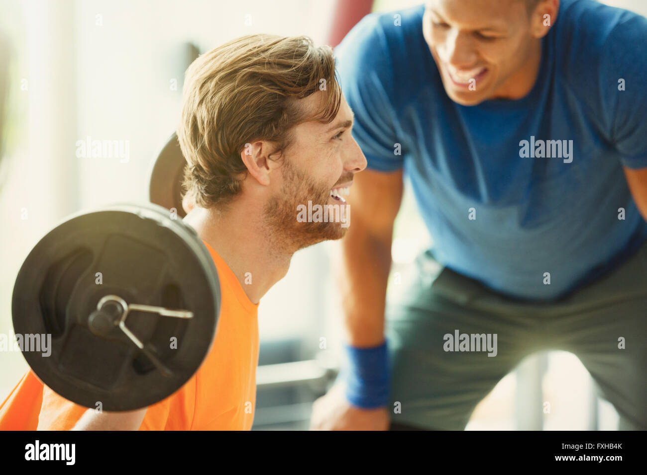 Personal trainer encouraging man doing barbell squats at gym Stock ...