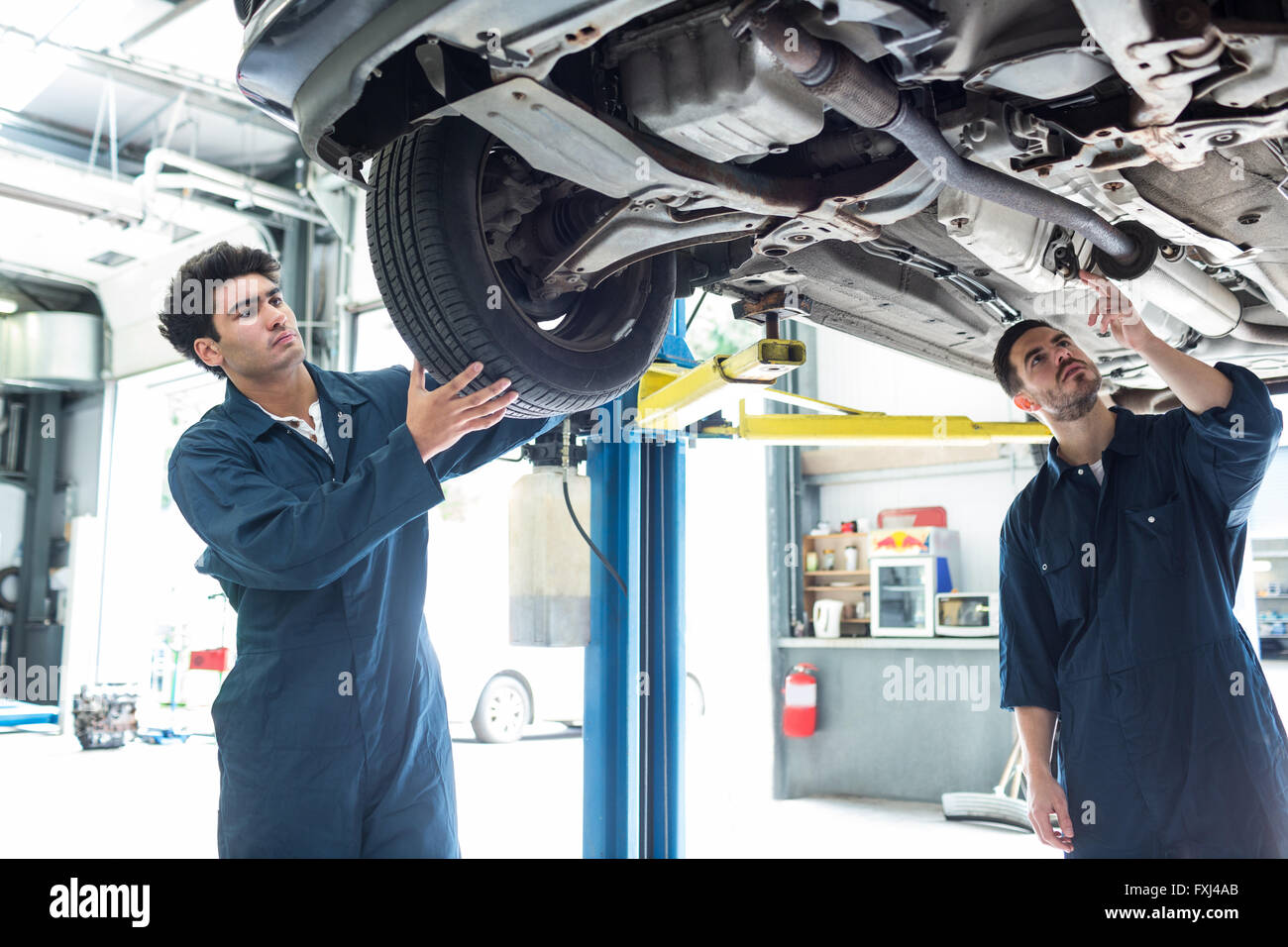 Mechanic fixing a wheel while a colleague examining car Stock Photo - Alamy