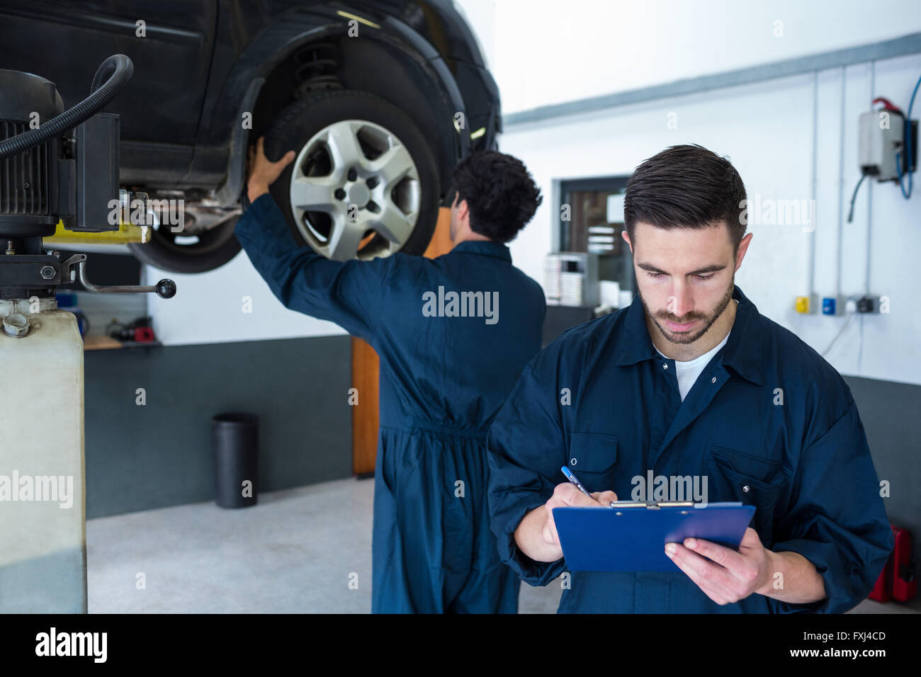 Mechanic preparing a check list while a colleague fixing cars wheel at ...