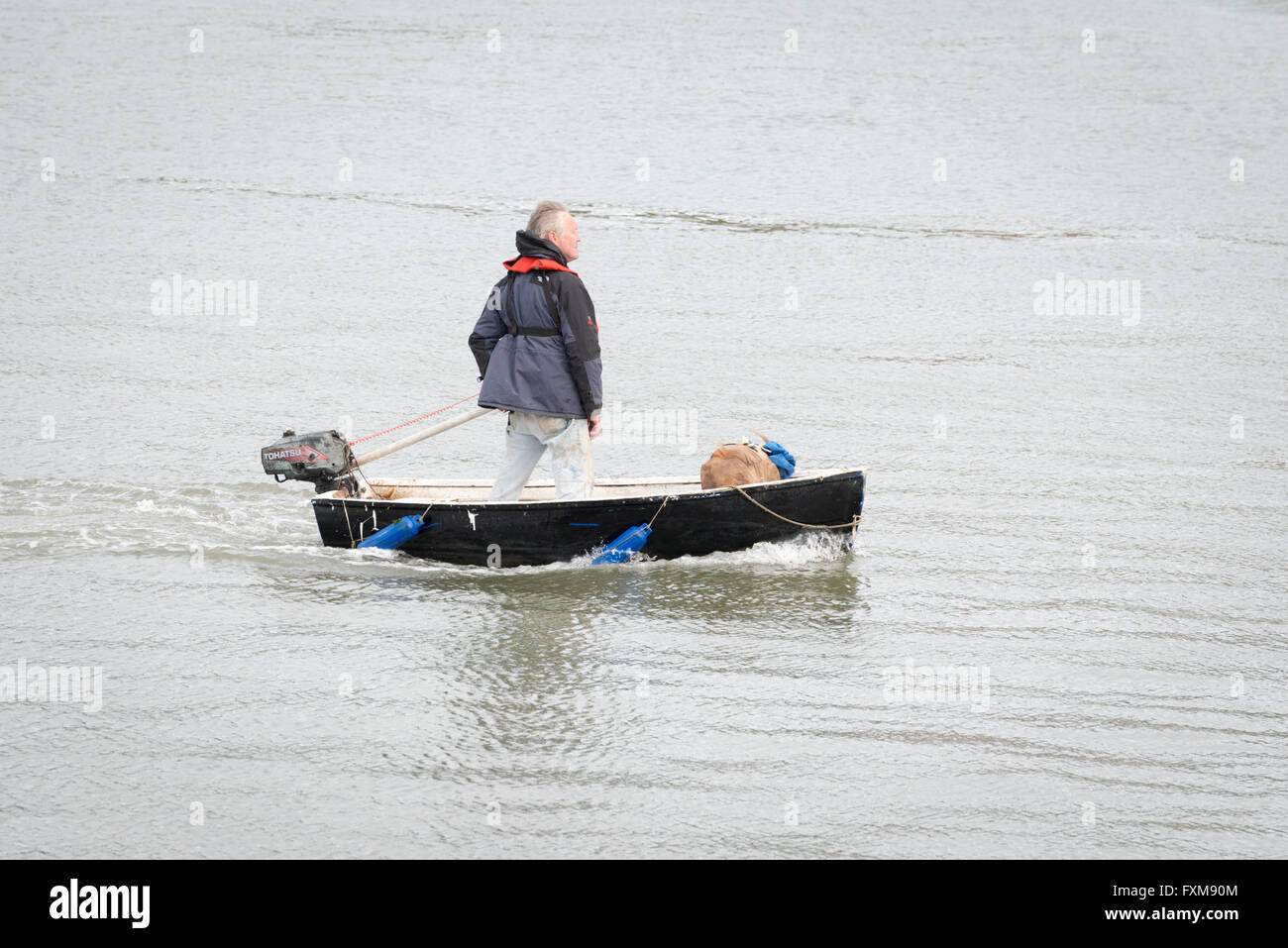 A large man standing in a small boat or tender driving along with an ...