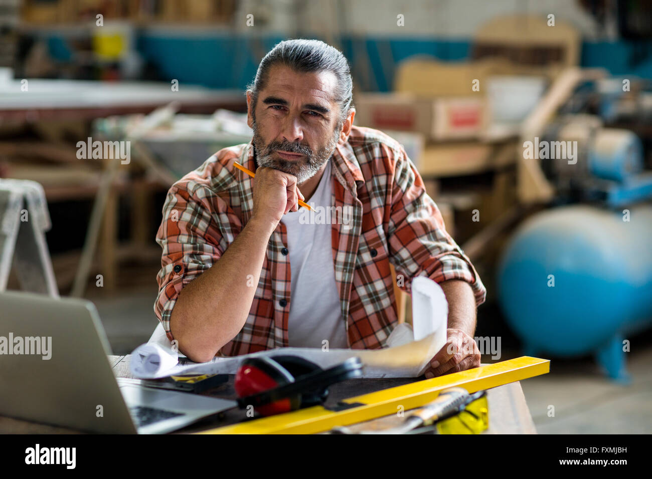 Portrait of carpenter sitting on workbench with blueprint in workshop ...