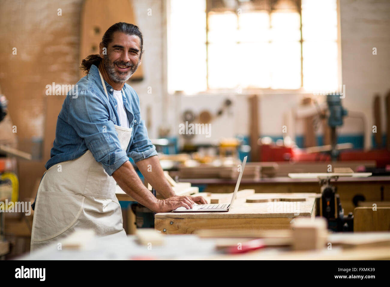 Portrait of carpenter standing in workshop and using laptop Stock Photo ...