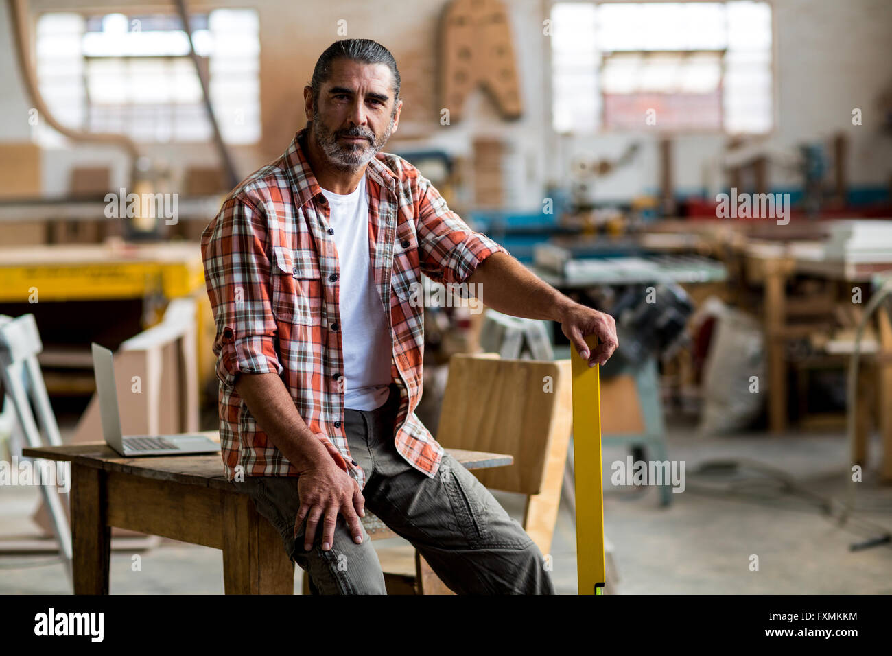 Portrait of confident carpenter sitting on table Stock Photo - Alamy