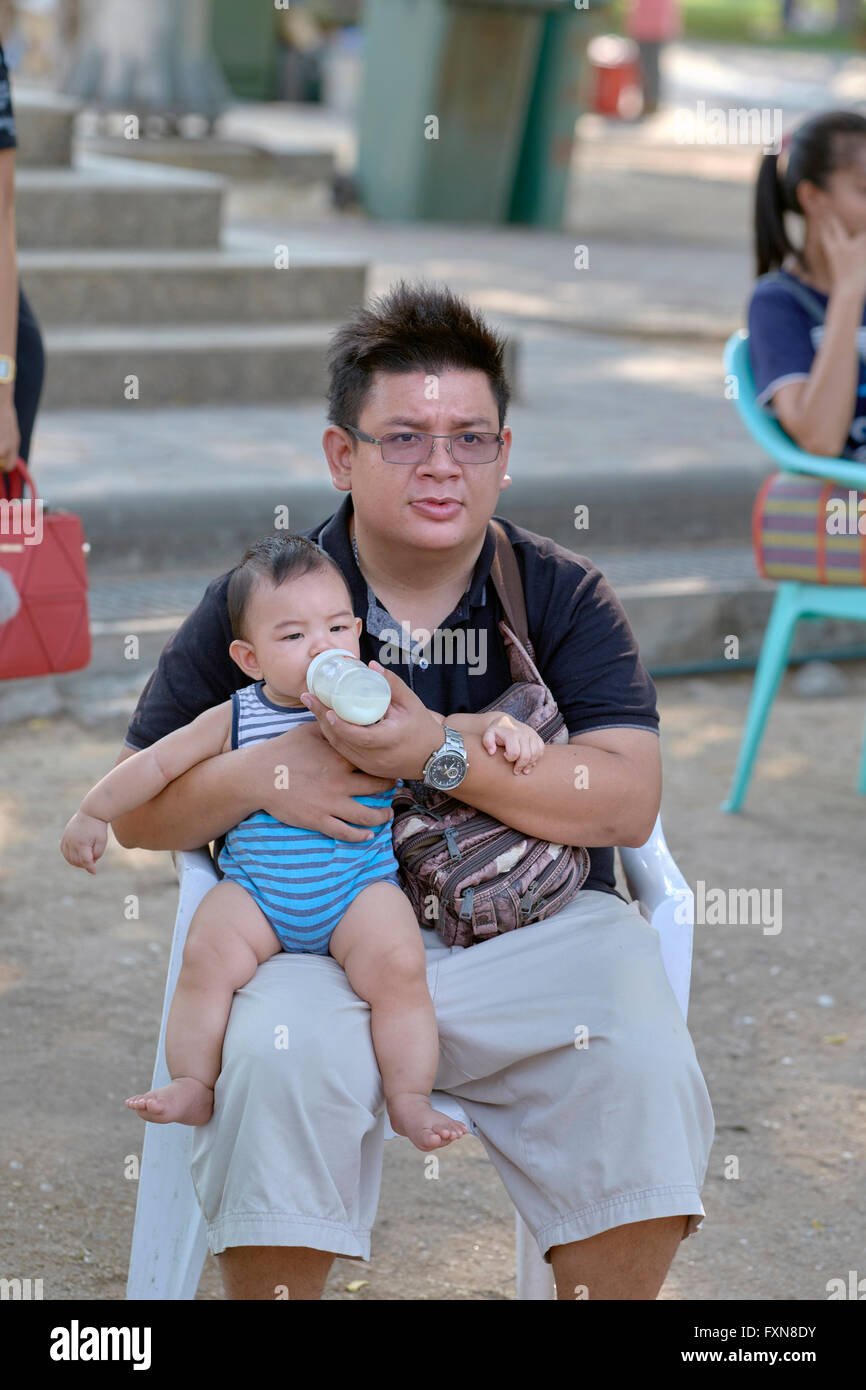 Father bottle feeding his infant child. Thailand S. E. Asia Stock Photo ...