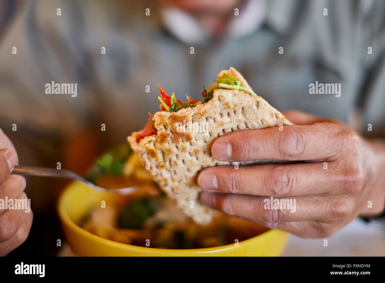 Man's hand holding a half eaten flatbread sandwich over a bowl of soup ...