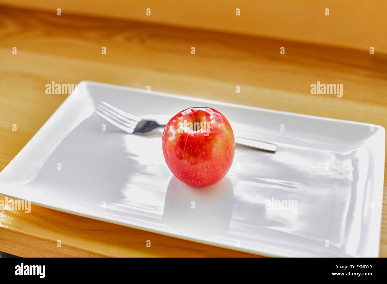 Red Apple on white rectangular plate with a silver fork in shallow ...