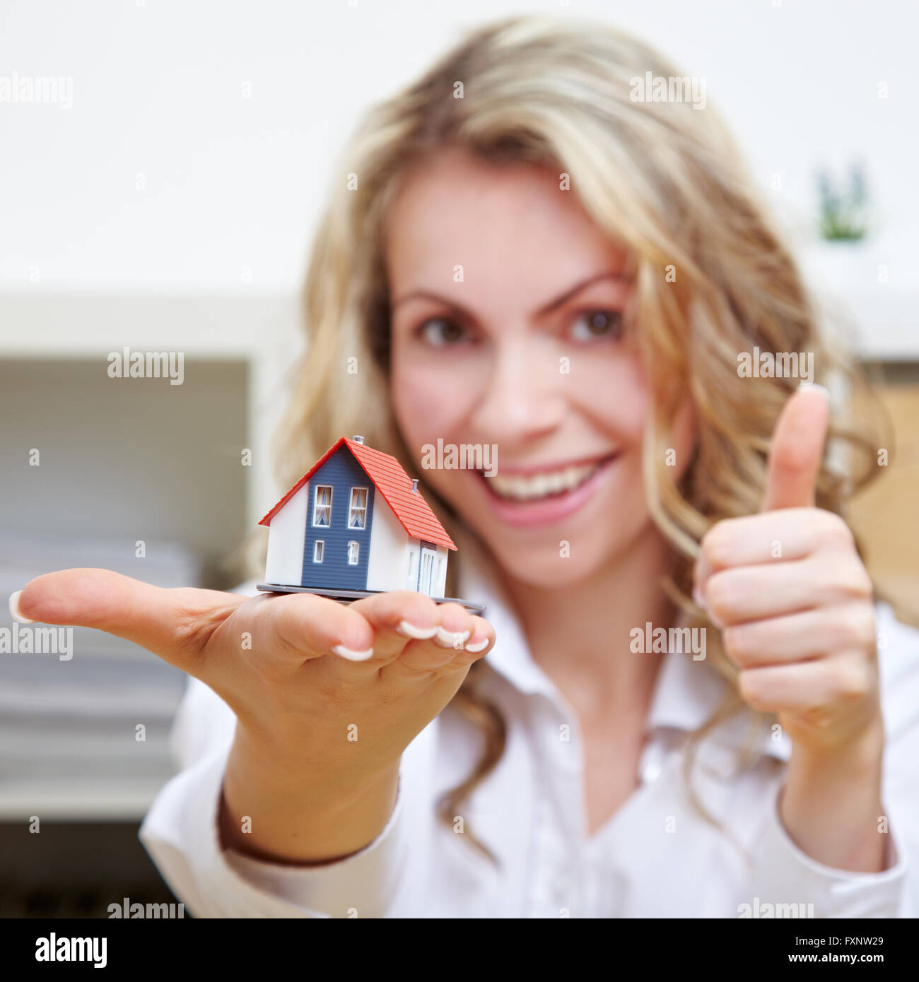 Smiling blonde woman with little house holding her thumbs up Stock ...
