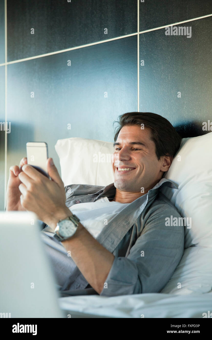 Man relaxing in bed with multimedia smartphone Stock Photo - Alamy