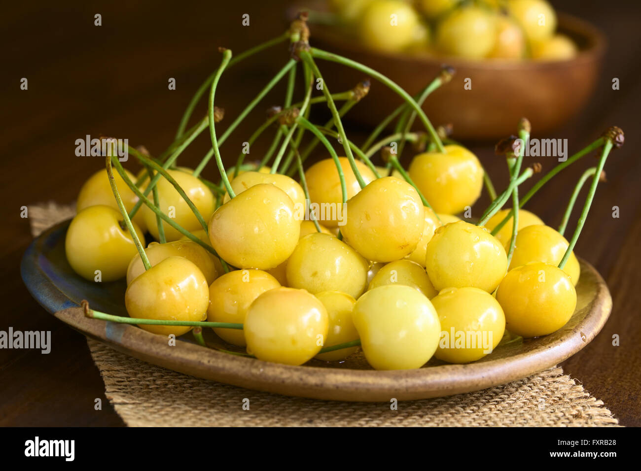Ripe yellow or Rainier cherry on plate, photographed on wood with ...