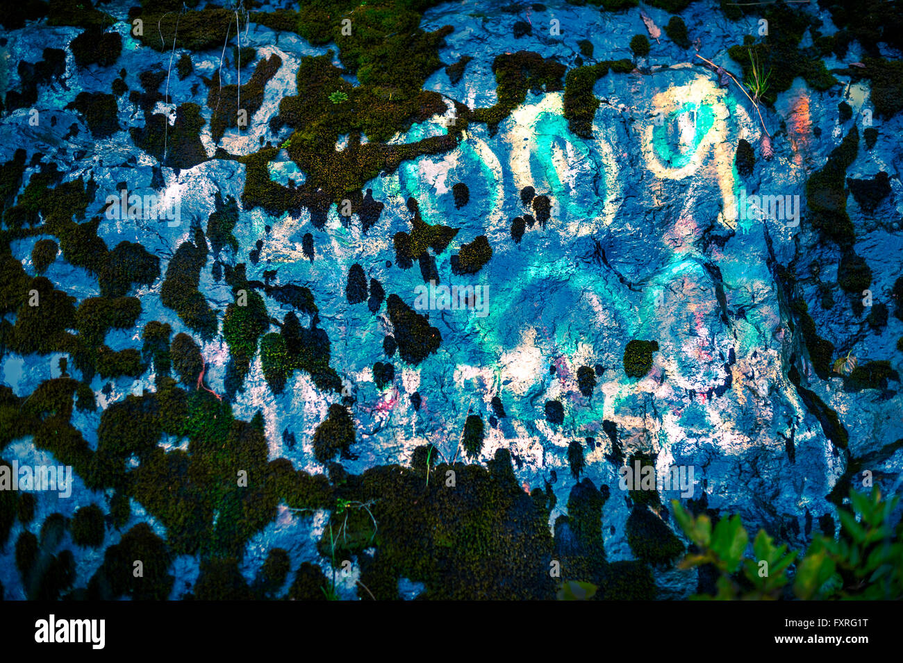 Graffiti overgrown by moss on rock cliff beside Sawmill Creek road near ...