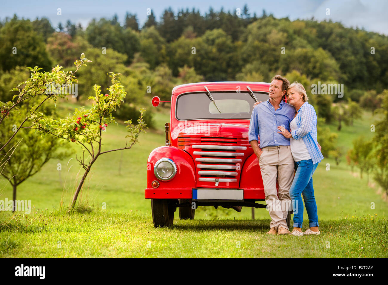 Senior couple hugging, vintage styled red car, sunny nature Stock Photo ...