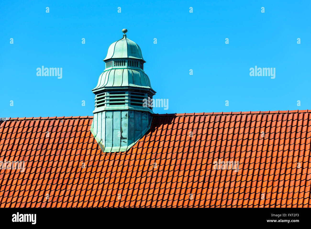 Small copper tower on top of a tiled roof with blue sky in background ...