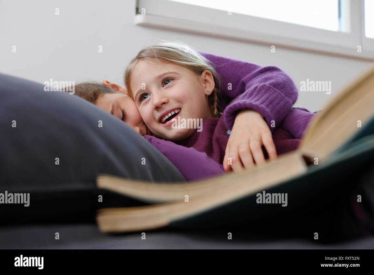 Surface level view of girl lying down on sofa with book, hugging and ...