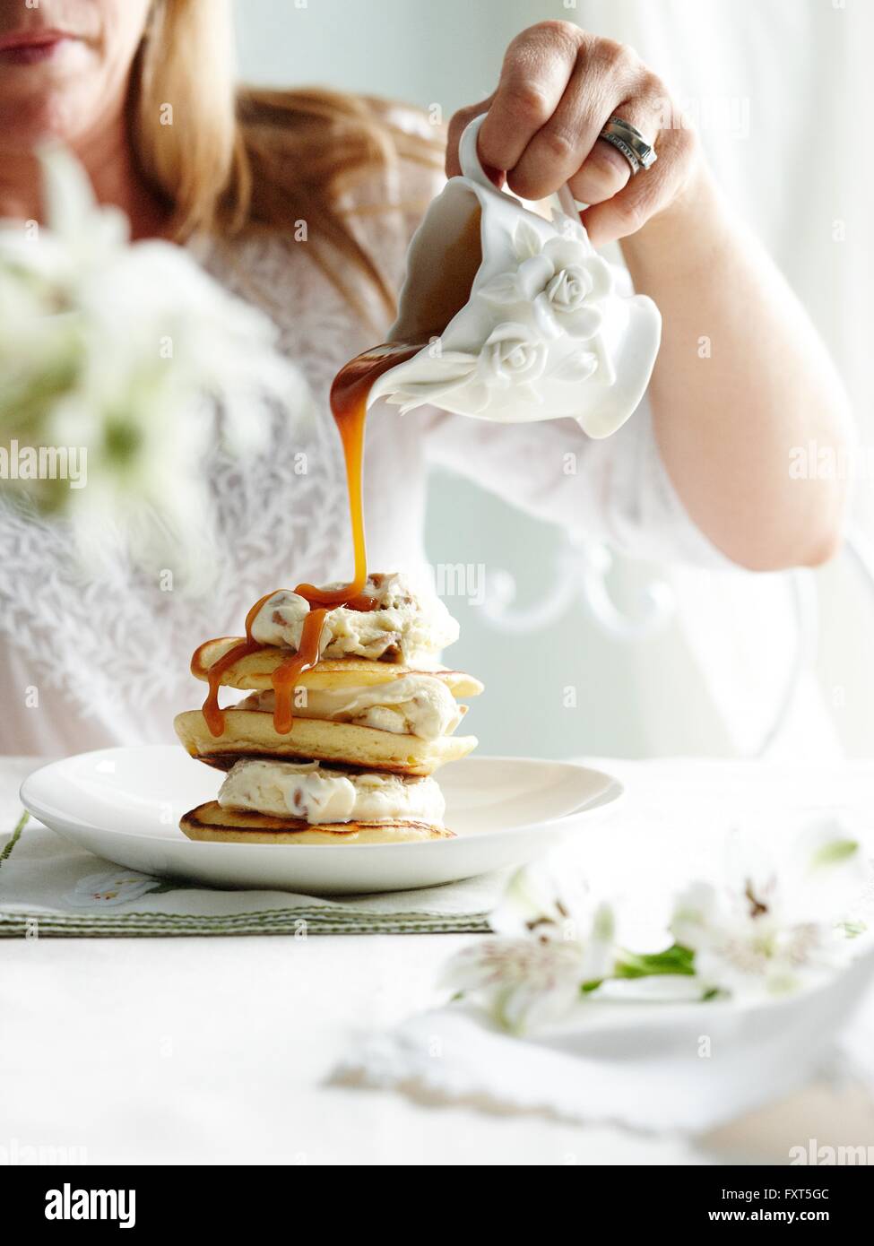 Woman pouring toffee sauce from ornate jug on stack of pikelets Stock ...