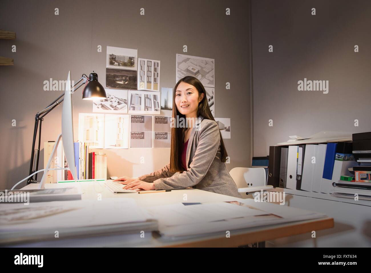 Side view of mid adult woman at desk using computer looking at camera ...